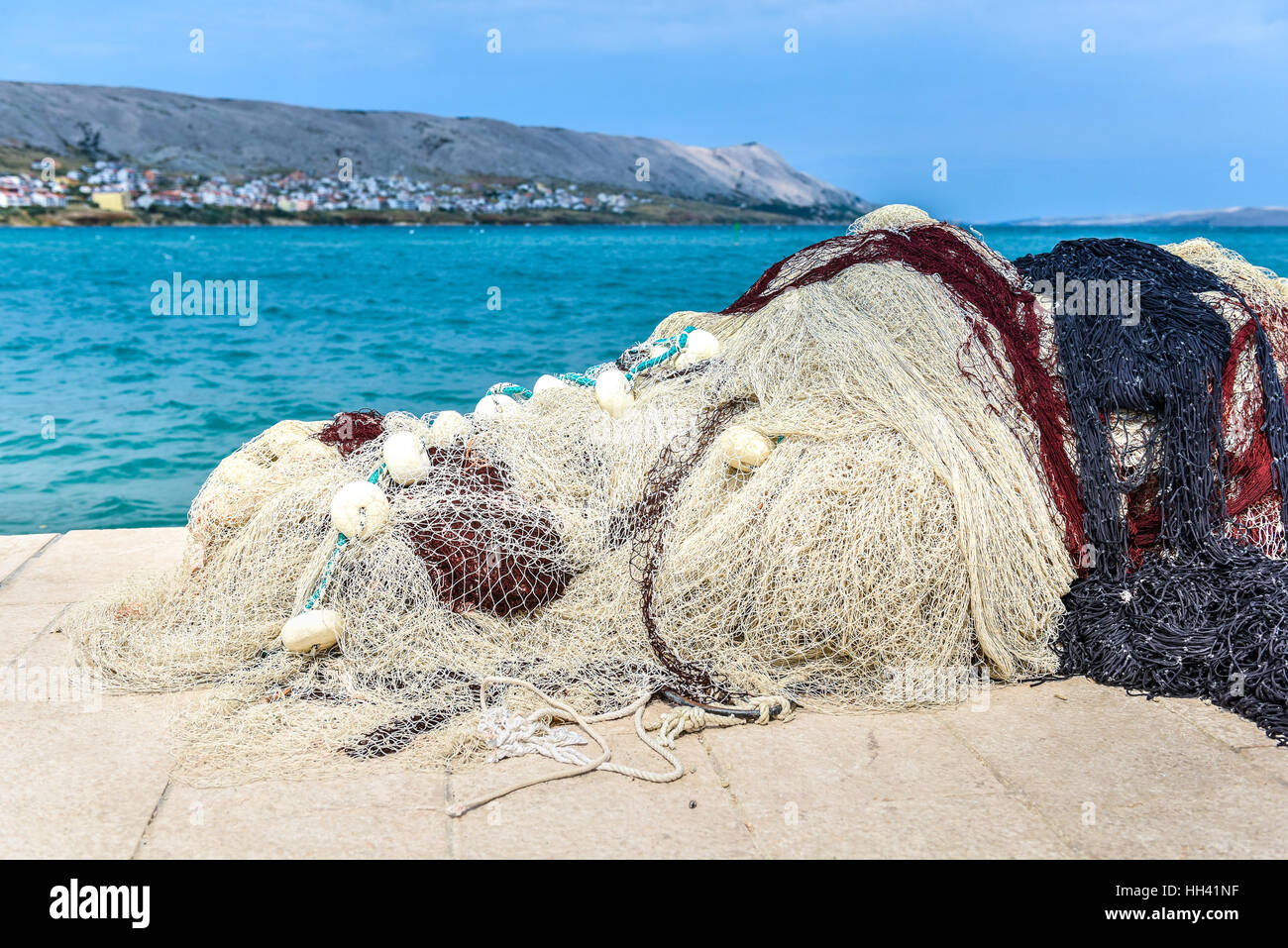 Stacked and piled fishing nets in a pier with blue sea in the back ...