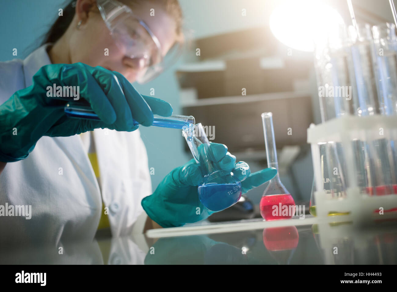 Young laboratory assistant with flasks and tubes on tripod at desk ...