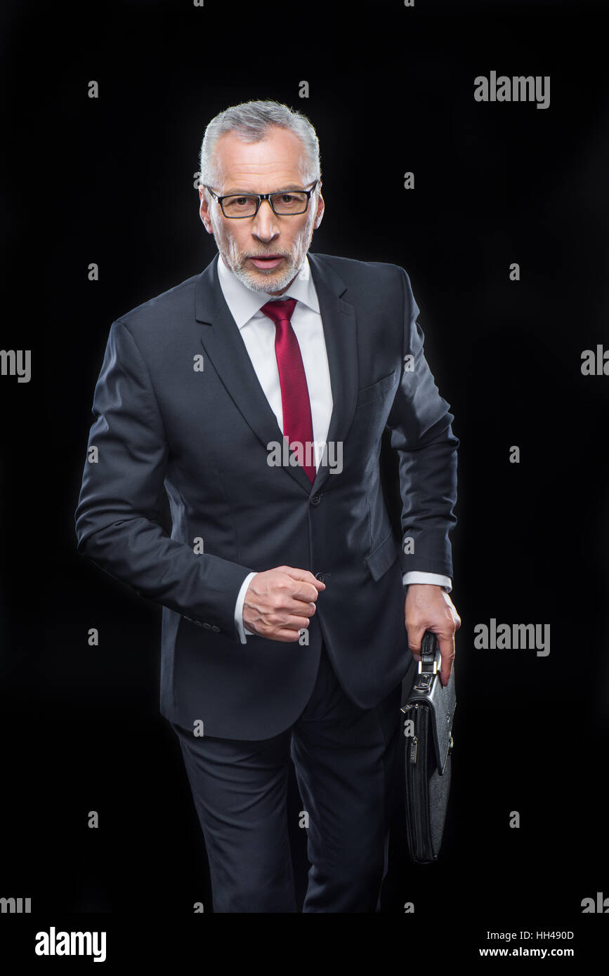 Mature businessman holding briefcase and running on black Stock Photo ...