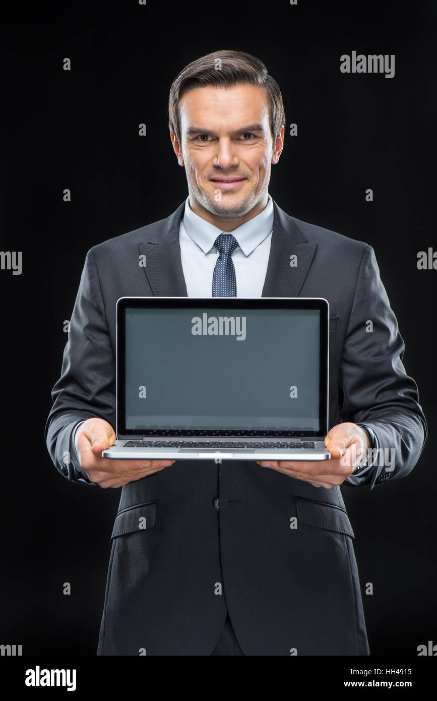 Businessman showing laptop with blank screen and smiling at camera ...
