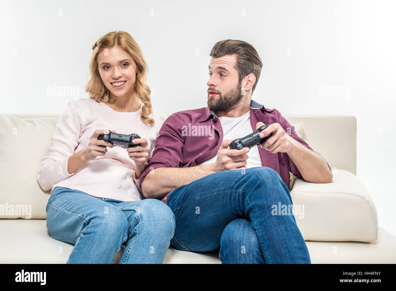 Smiling young couple sitting on couch and playing video games with ...