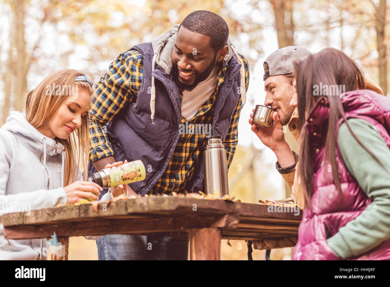 Group of smiling friends sitting at wooden table and pouring hot drink ...