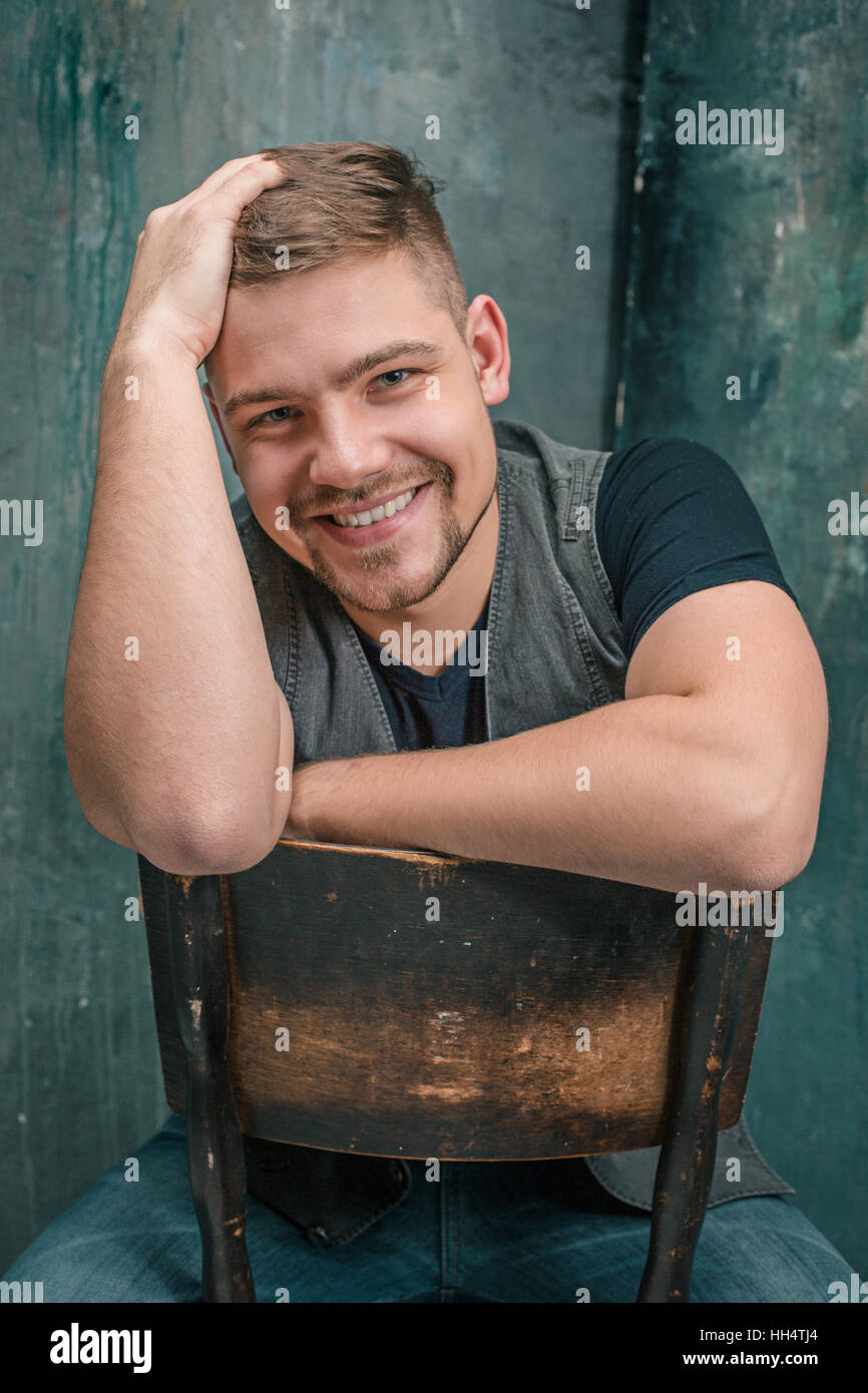 Portrait of smiling happy man sitting on the wooden chair on gray ...
