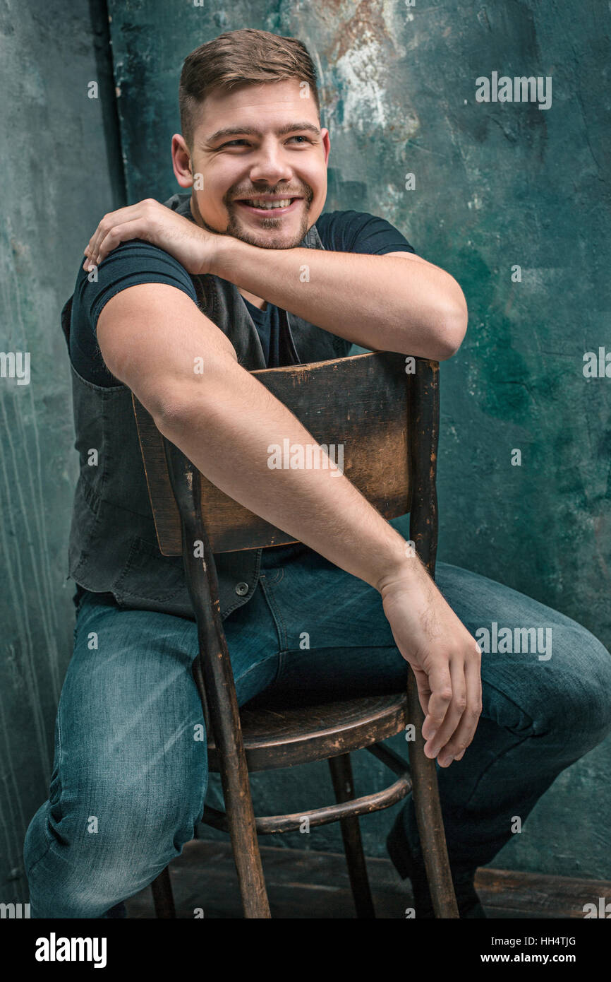 Portrait of smiling happy man sitting on the wooden chair on gray ...