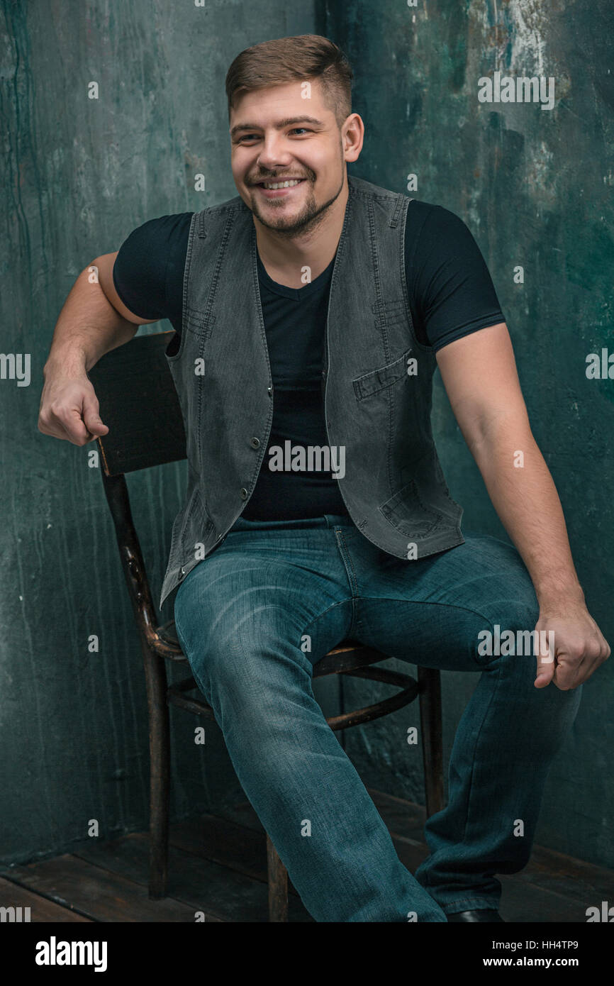 Portrait of smiling happy man sitting on the wooden chair on gray ...