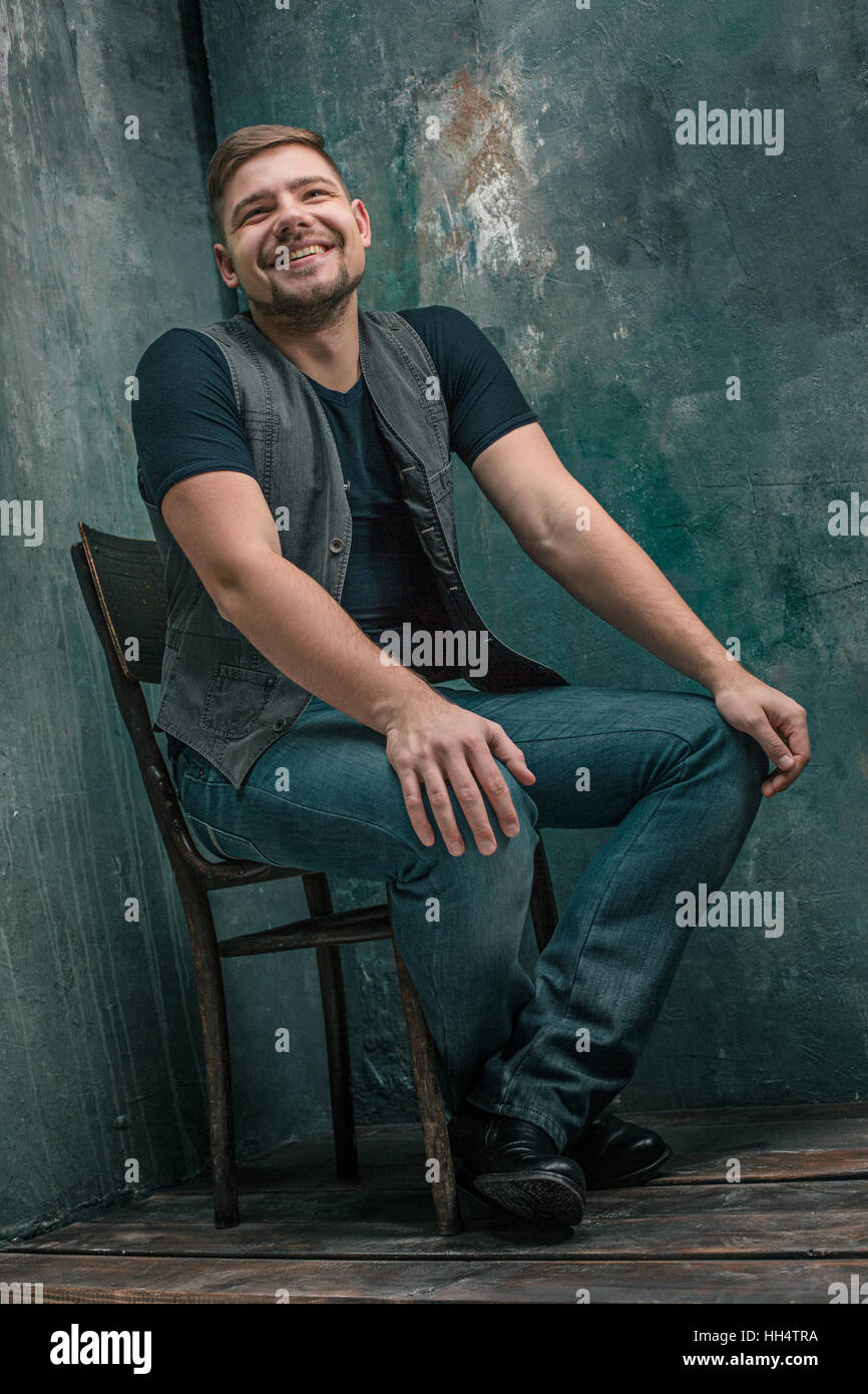 Portrait of smiling happy man sitting on the wooden chair on gray ...