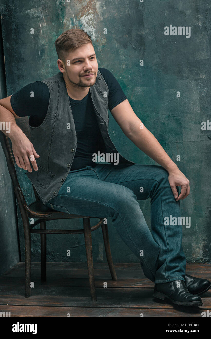 Portrait of smiling happy man sitting on the wooden chair on gray ...