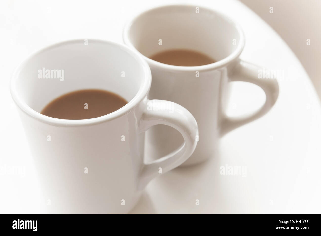 Two big cups full of coffee with milk stand on white table, closeup ...