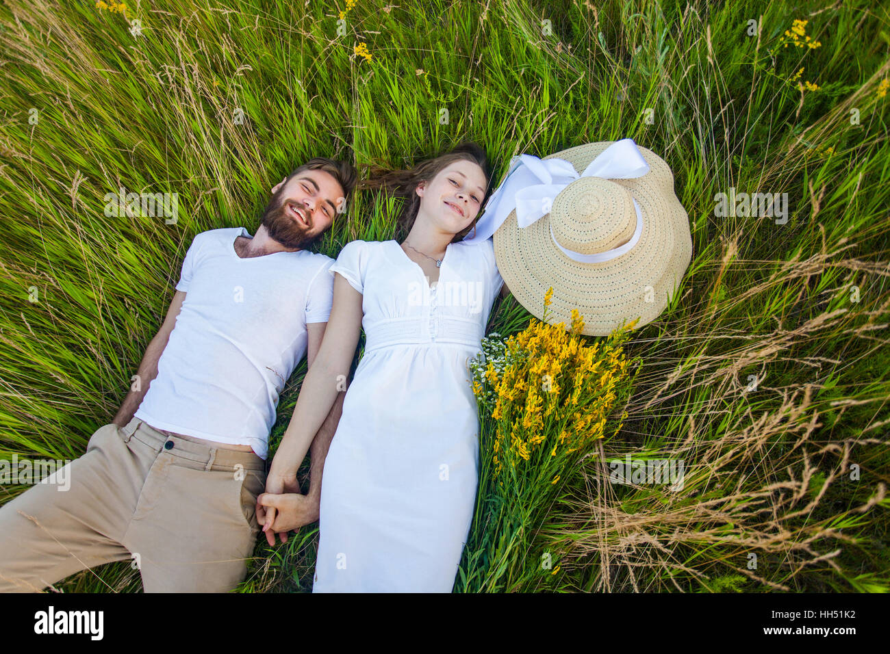Happy young relaxed couple in love laying down on the grass overhead ...