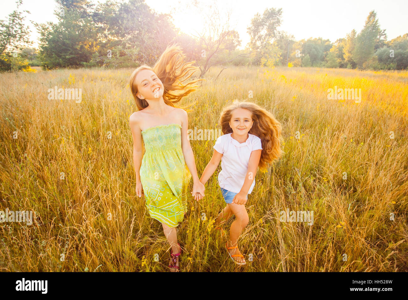 Two beautiful sisters running on the lawn in the nature park outdoor in ...