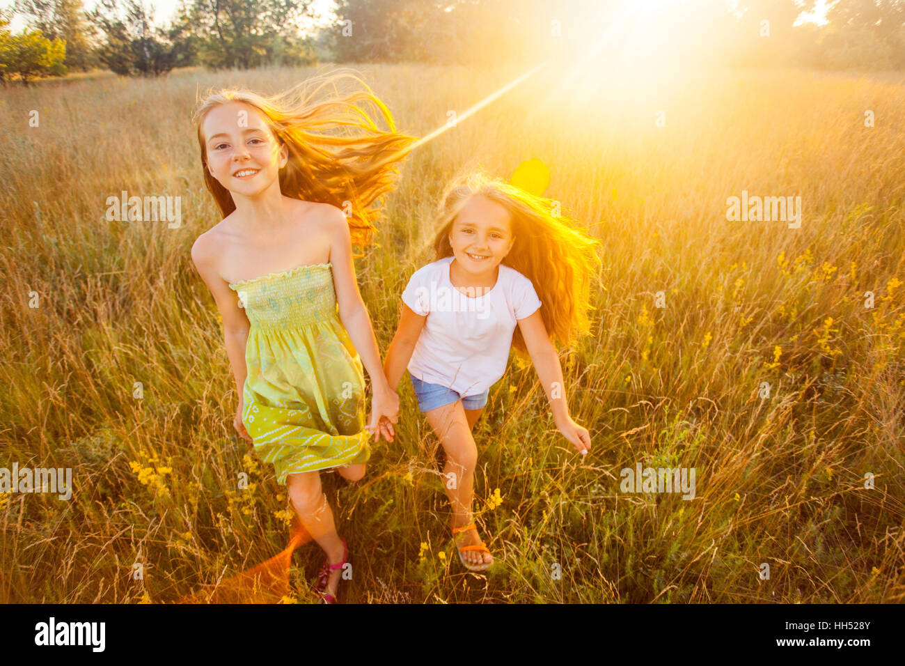 Two beautiful sisters running on the lawn in the nature park outdoor in ...