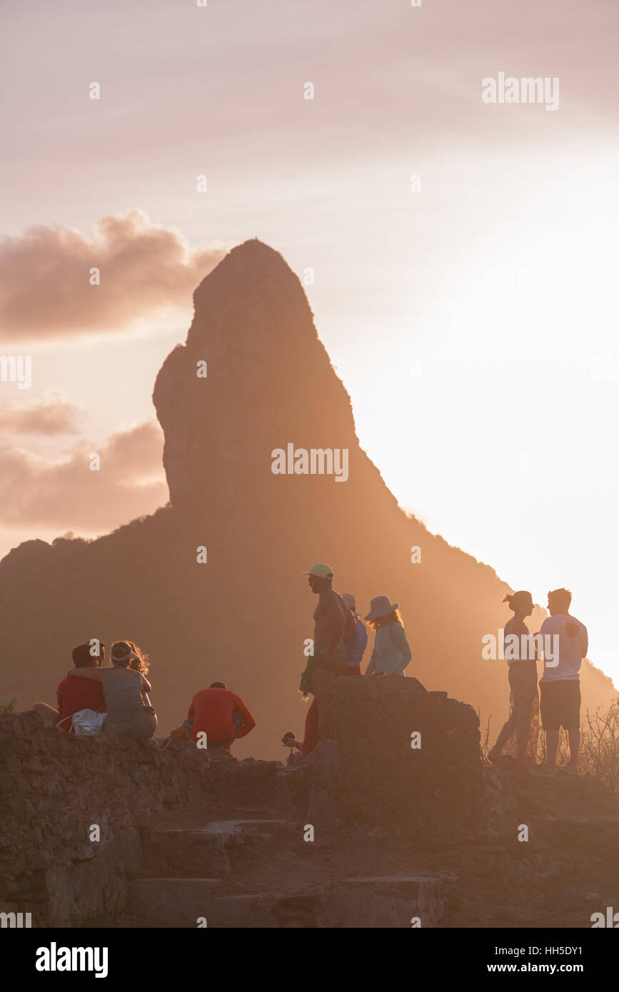 Couples watching the sunset behind the rock "Morro do Pico", island ...