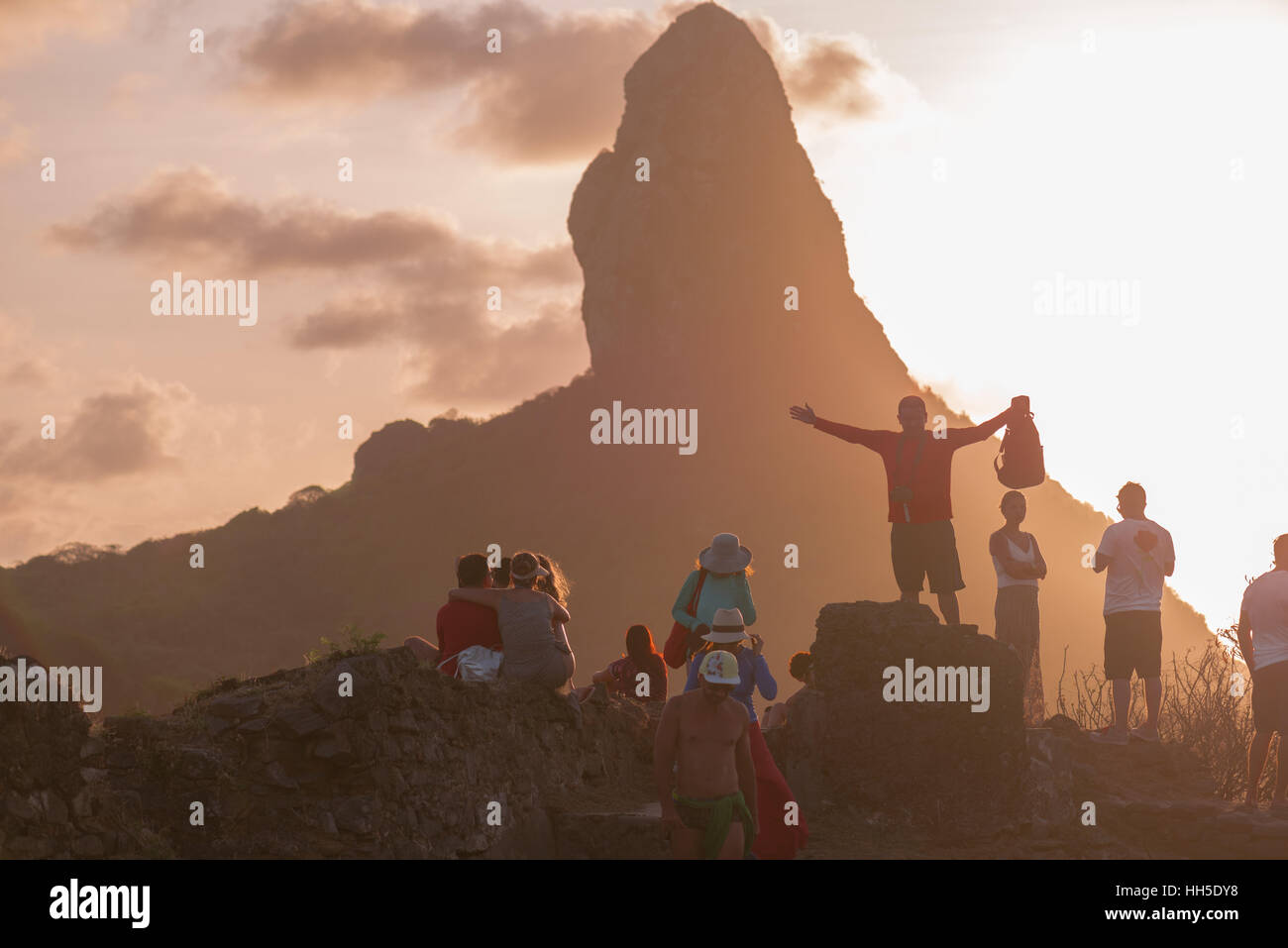 Couples watching the sunset behind the rock "Morro do Pico", island ...