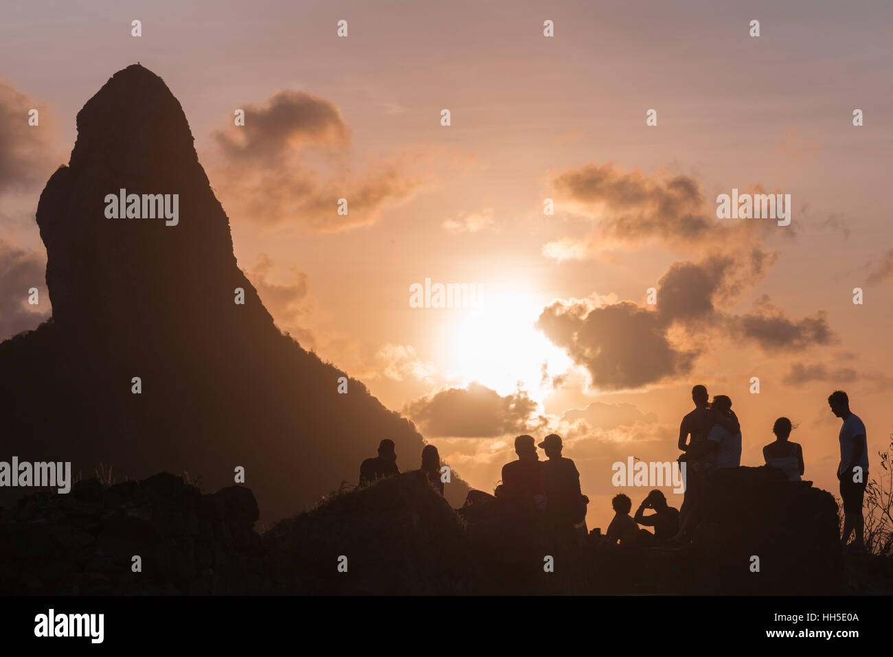 Couples watching the sunset behind the rock "Morro do Pico", island ...