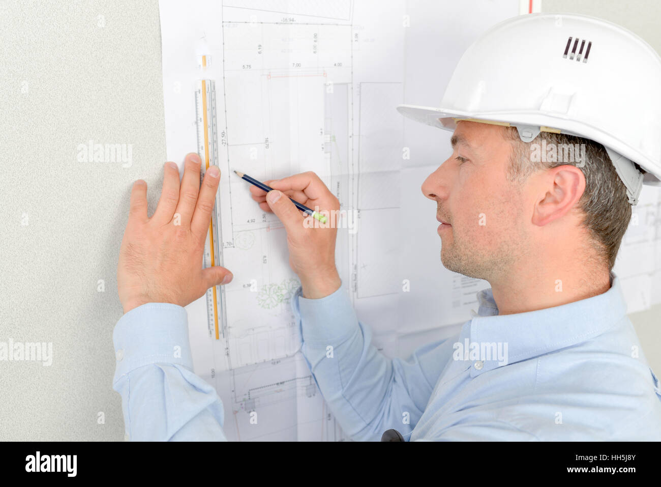 Man measuring plans pinned to wall Stock Photo - Alamy