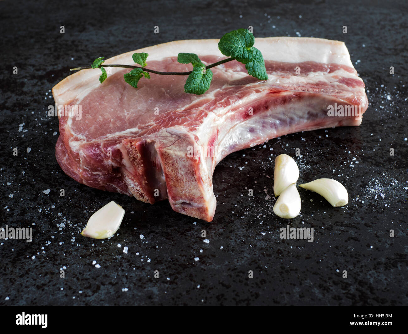 Raw pork chop, garlic, mint and salt on black stone background Stock ...