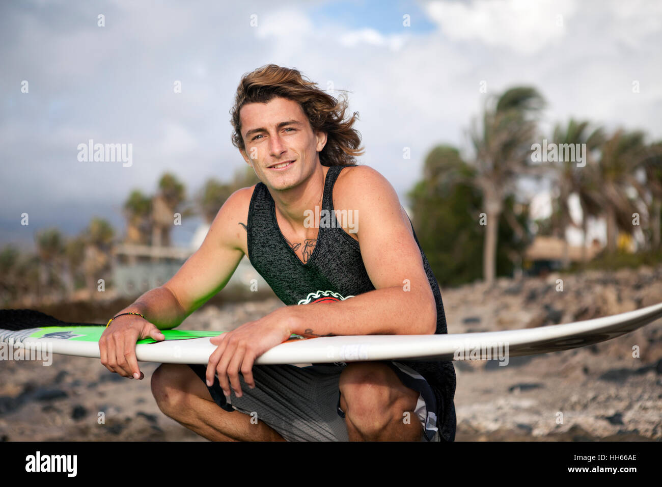 Young, smiling surfer holding a surfboard on the beach Stock Photo - Alamy