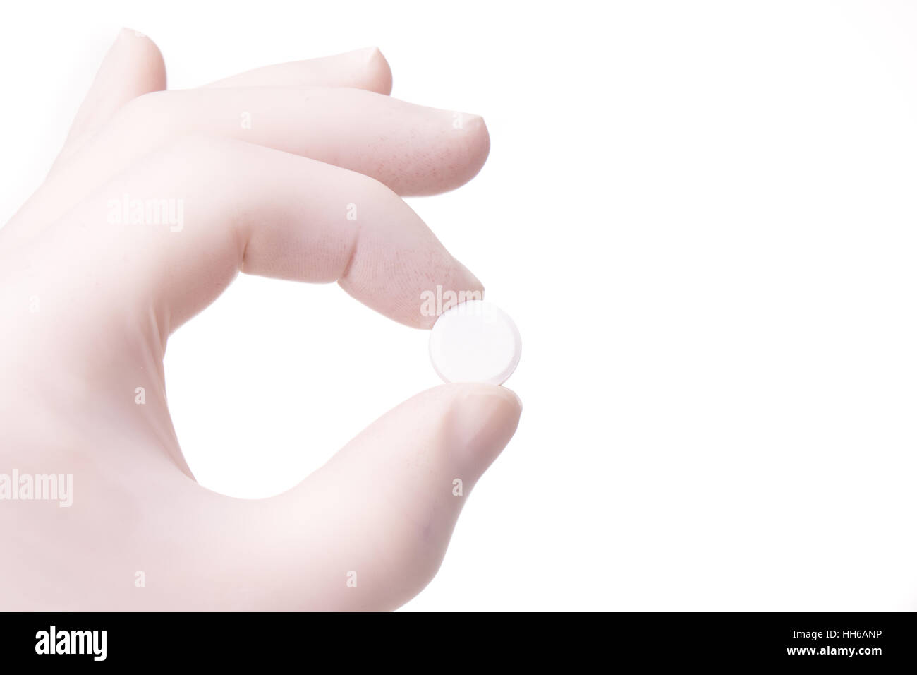 gloved hand holding small round pill. Hand and medicines are isolated ...