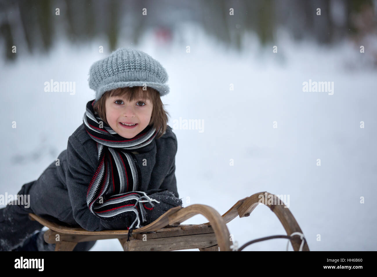 Cute little boy, lying down on sledge, smiling at camera, playing in ...