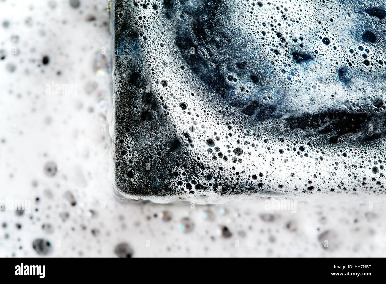 Black coal bar of soap in foam on dark background. Close-up composition ...