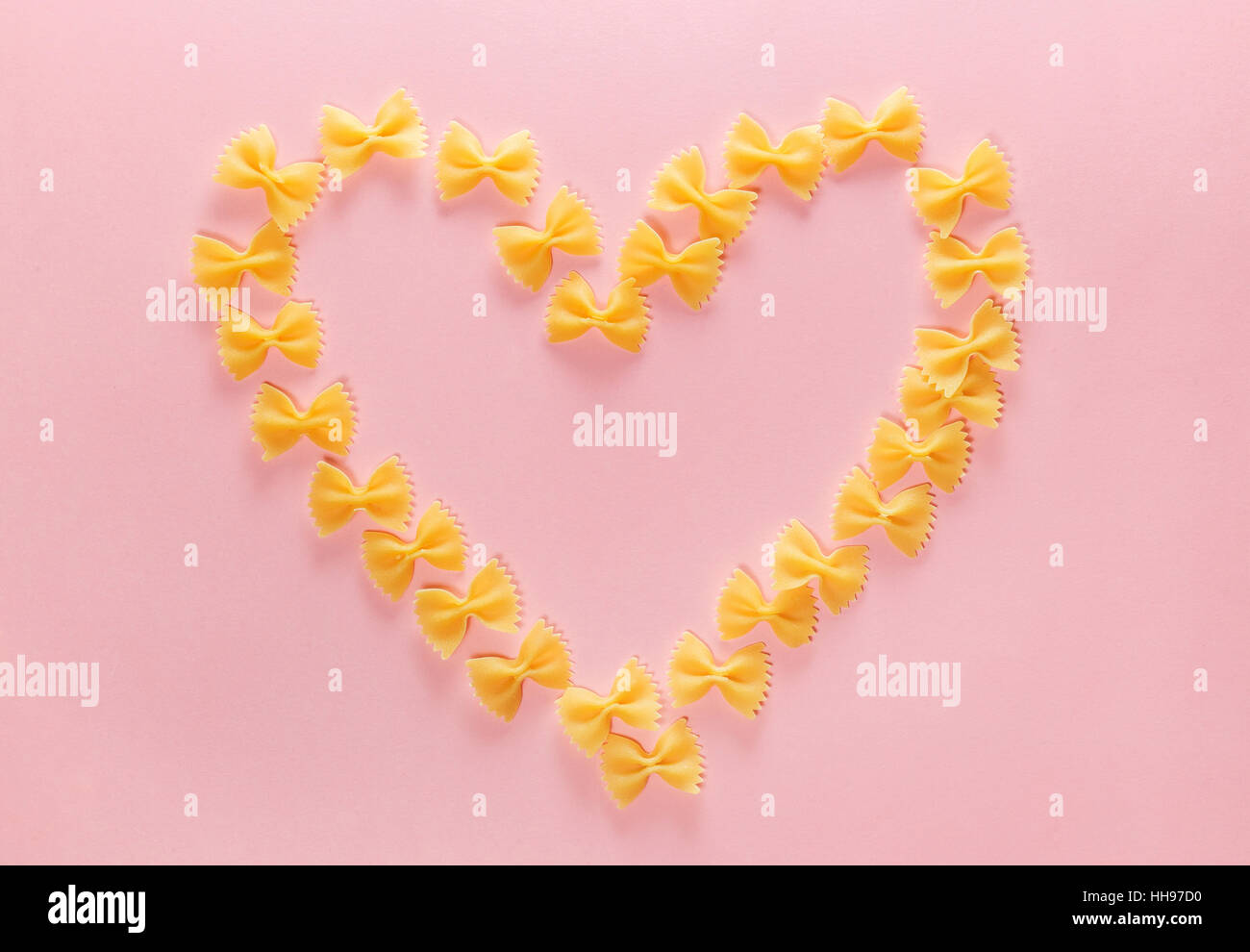 Heart frame from wheat pasta farfalle on rose background. Valentine's ...