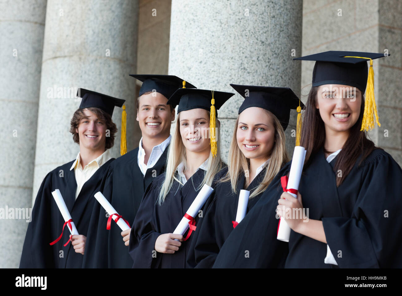 Smiling graduates posing in single line with columns in background ...