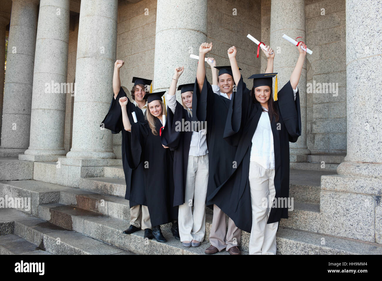 Five happy graduates posing the arms raised in front of the university ...