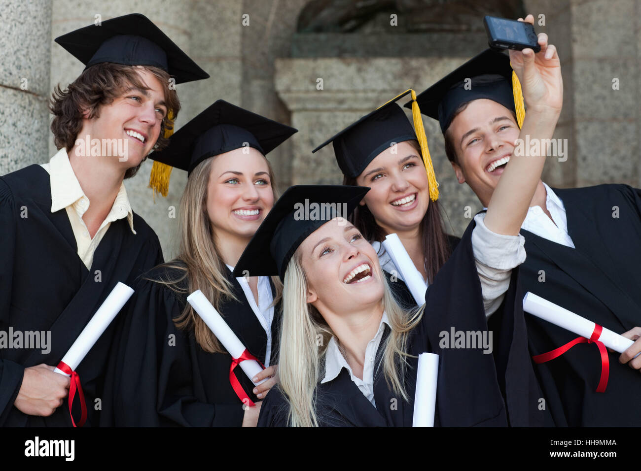 Close-up of happy graduates taking a picture of themselves in front of ...