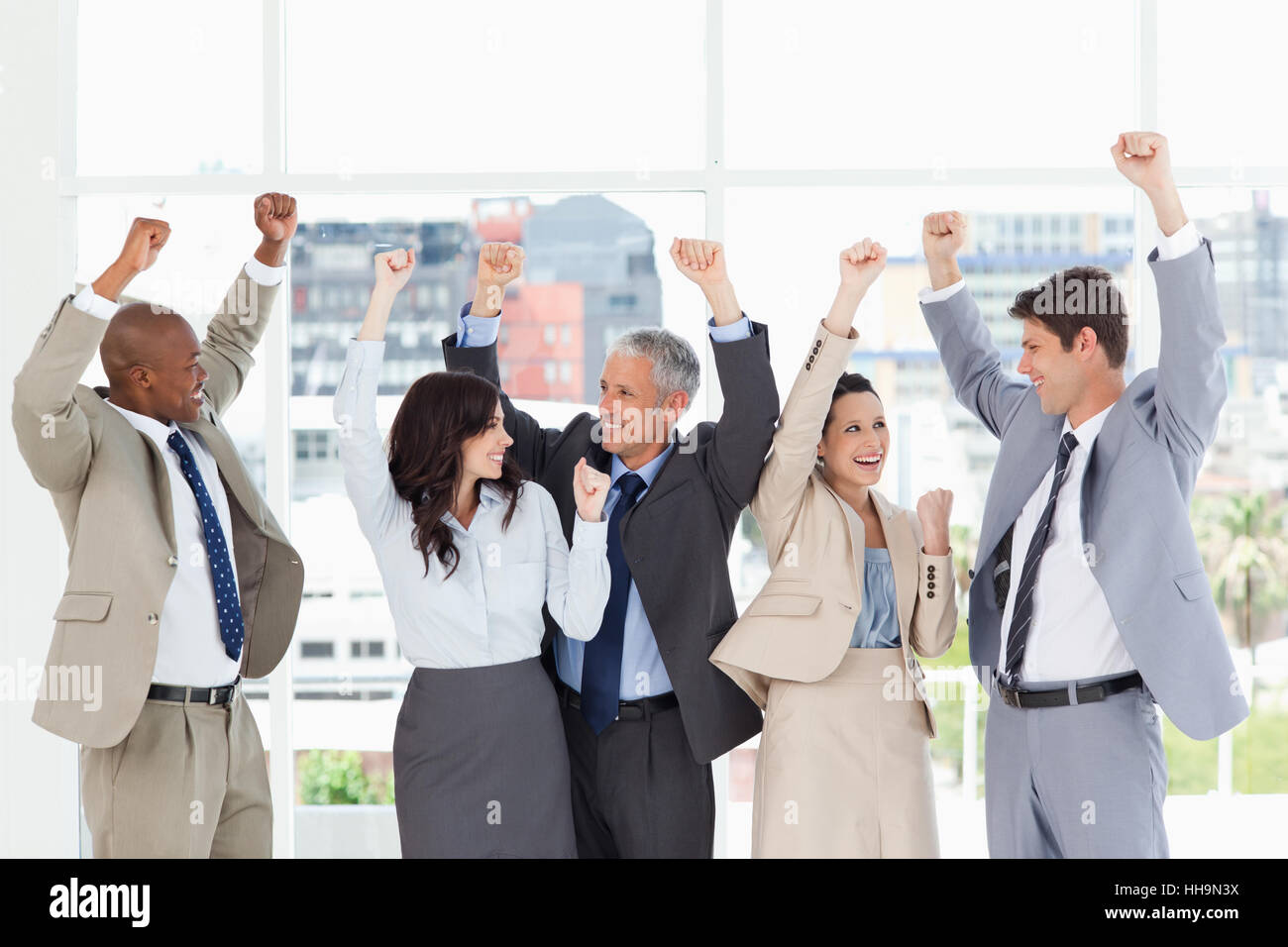 Smiling business people looking at each other and raising their arms in ...