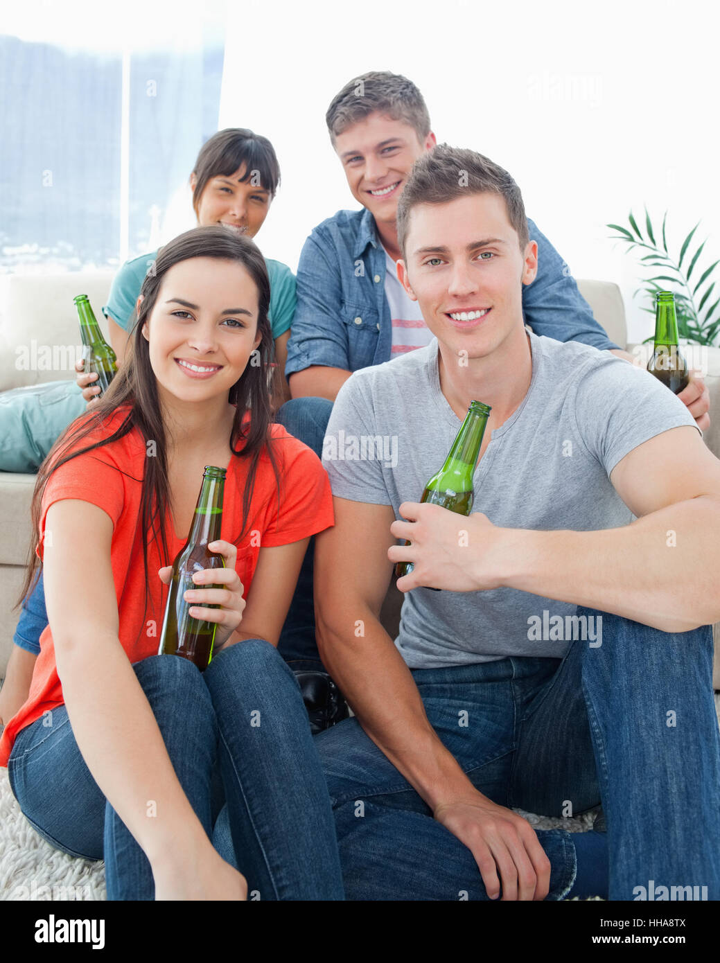 A smiling group of friends as one couple sit on the floor and the other ...