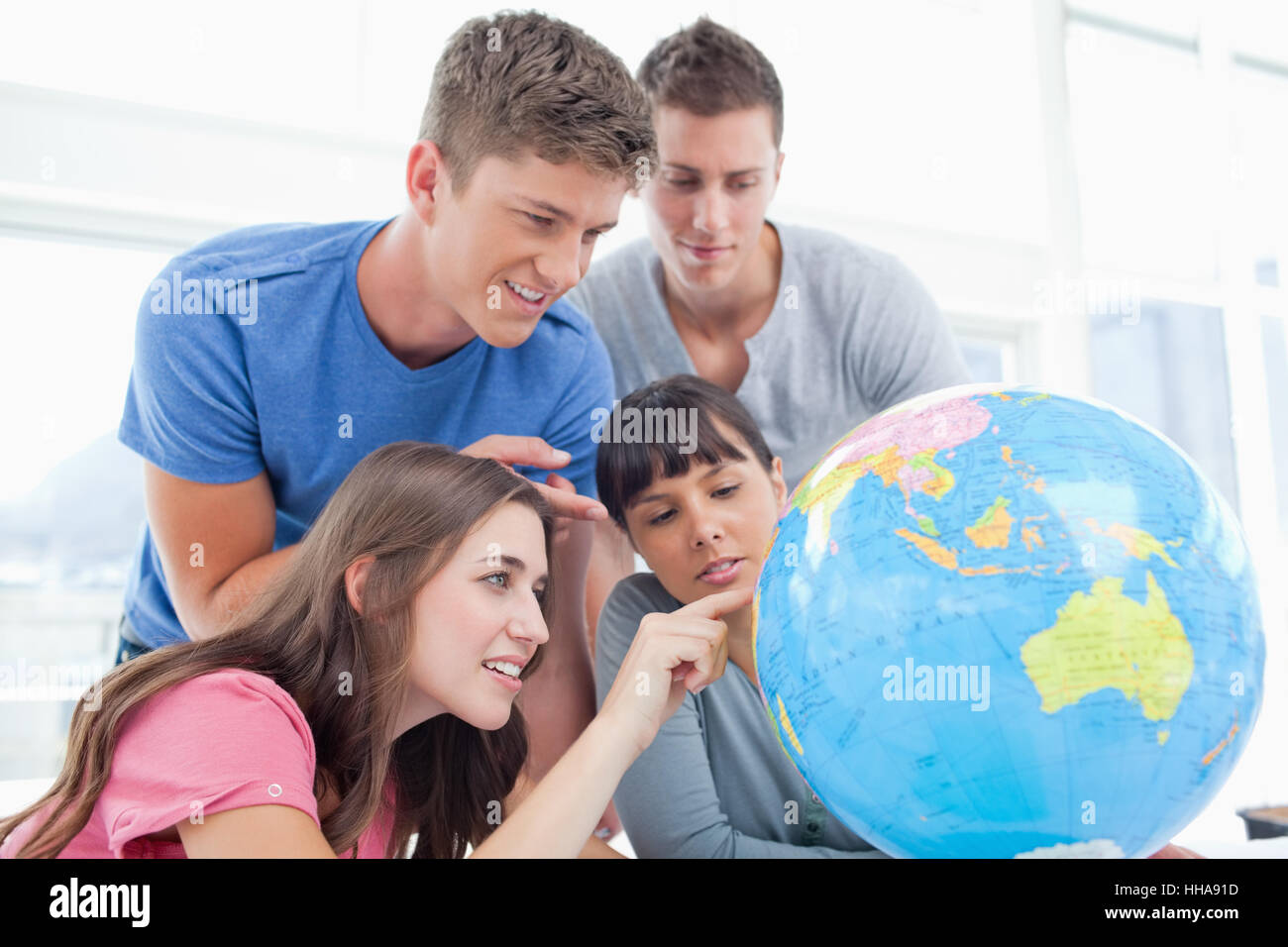 Four smiling students around a globe as two of them point to places in ...