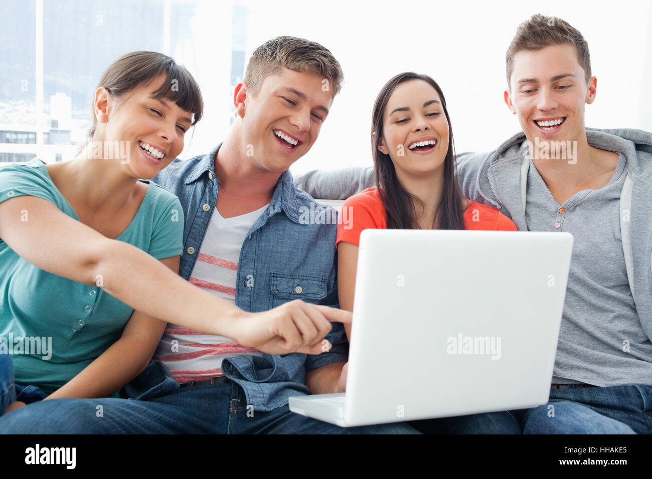 A laughing group of friends around a laptop watching the screen as they ...