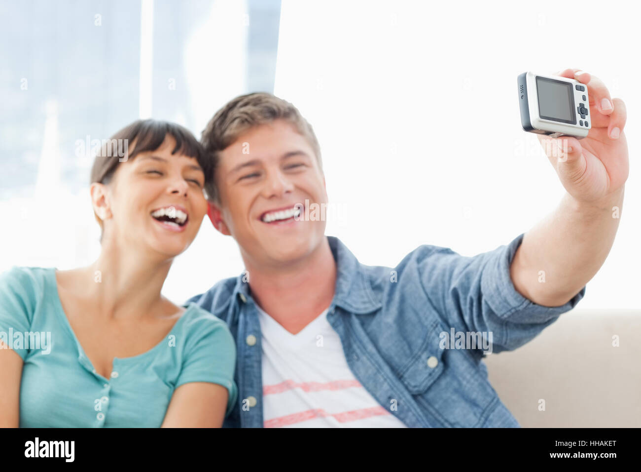 A couple pose together for a photo as they laugh while on the couch ...