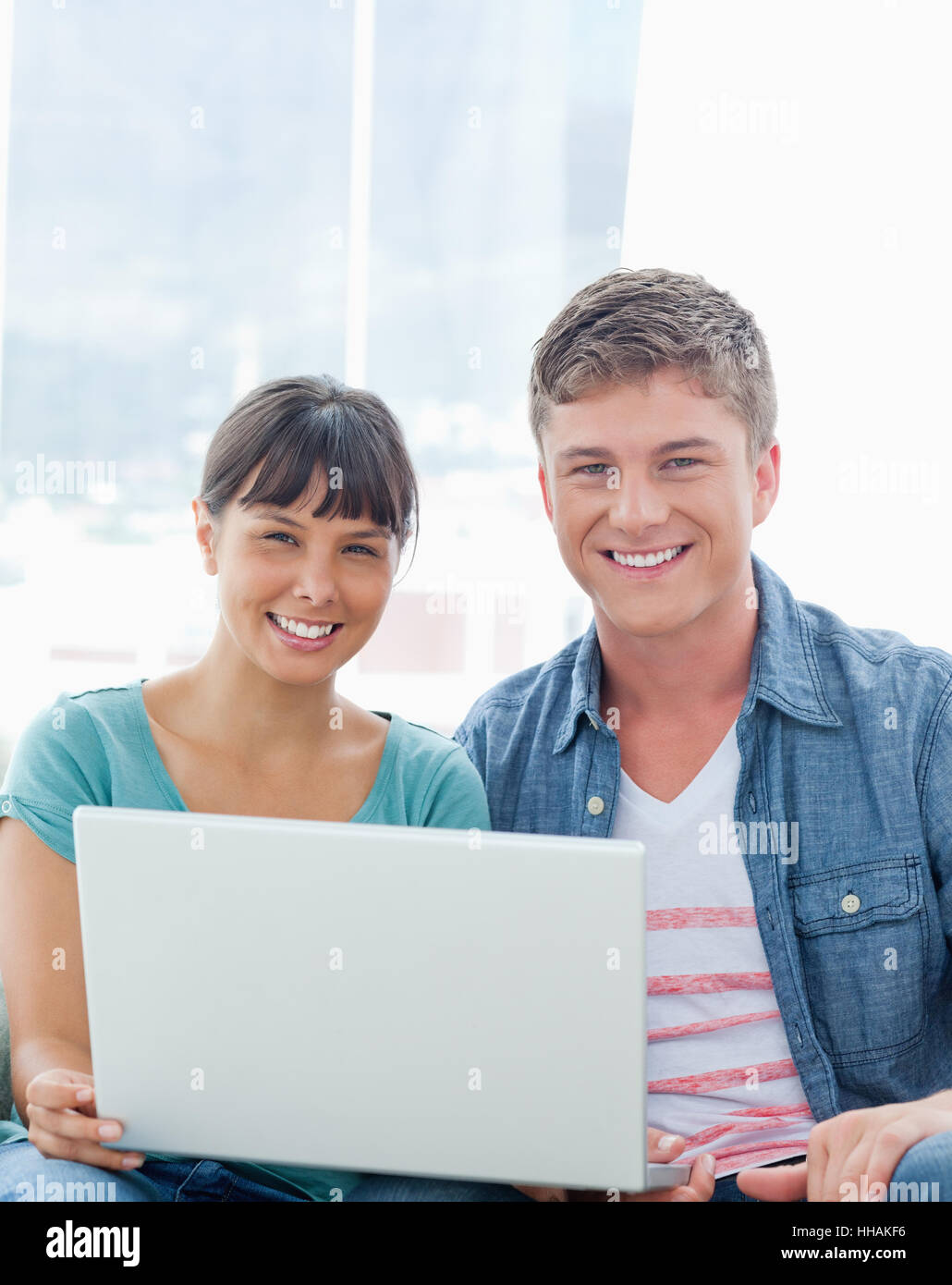 A couple with a laptop smiling as they look into the camera as they sit ...