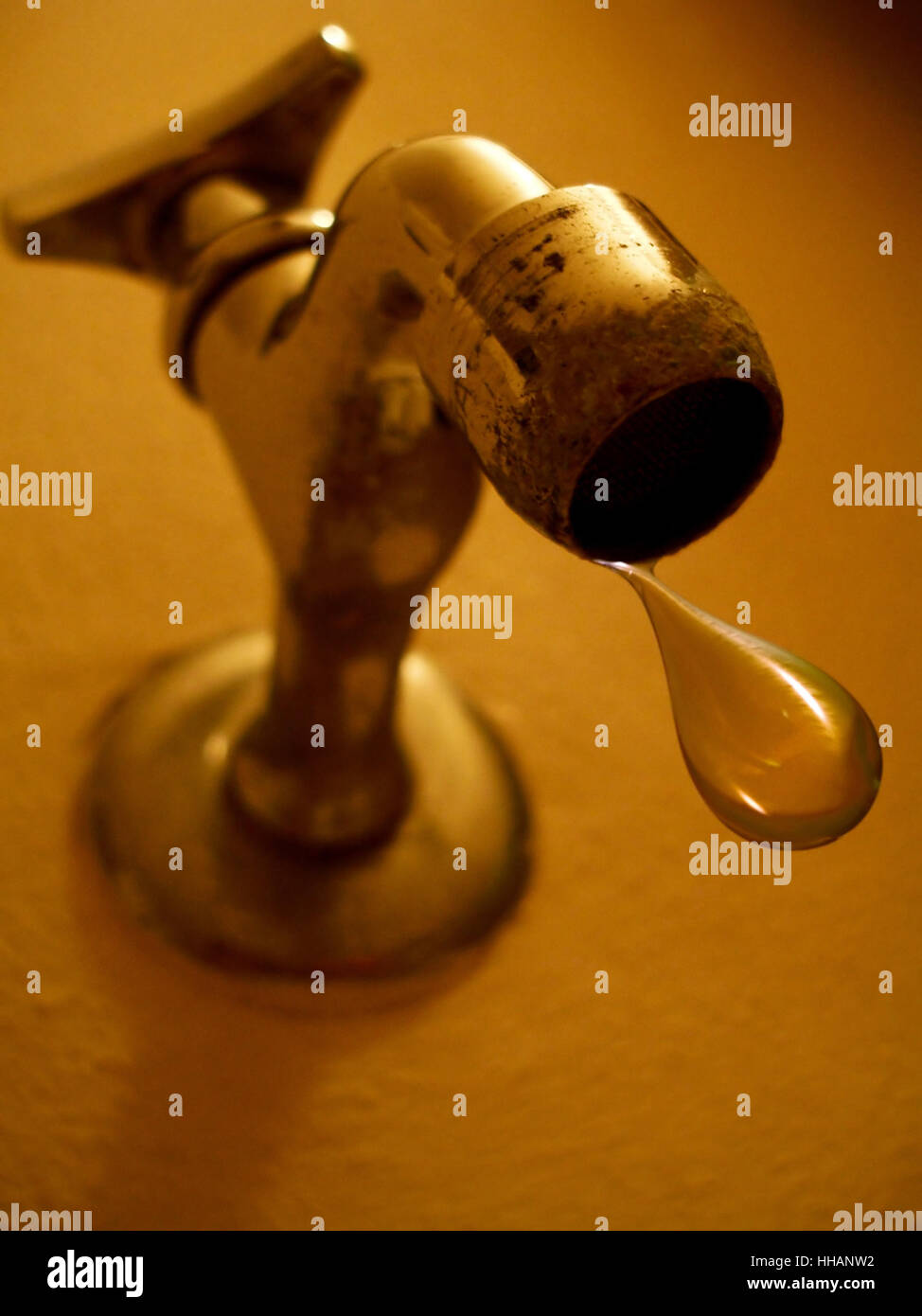 close up view of a large drip of water about to fall from an old faucet ...