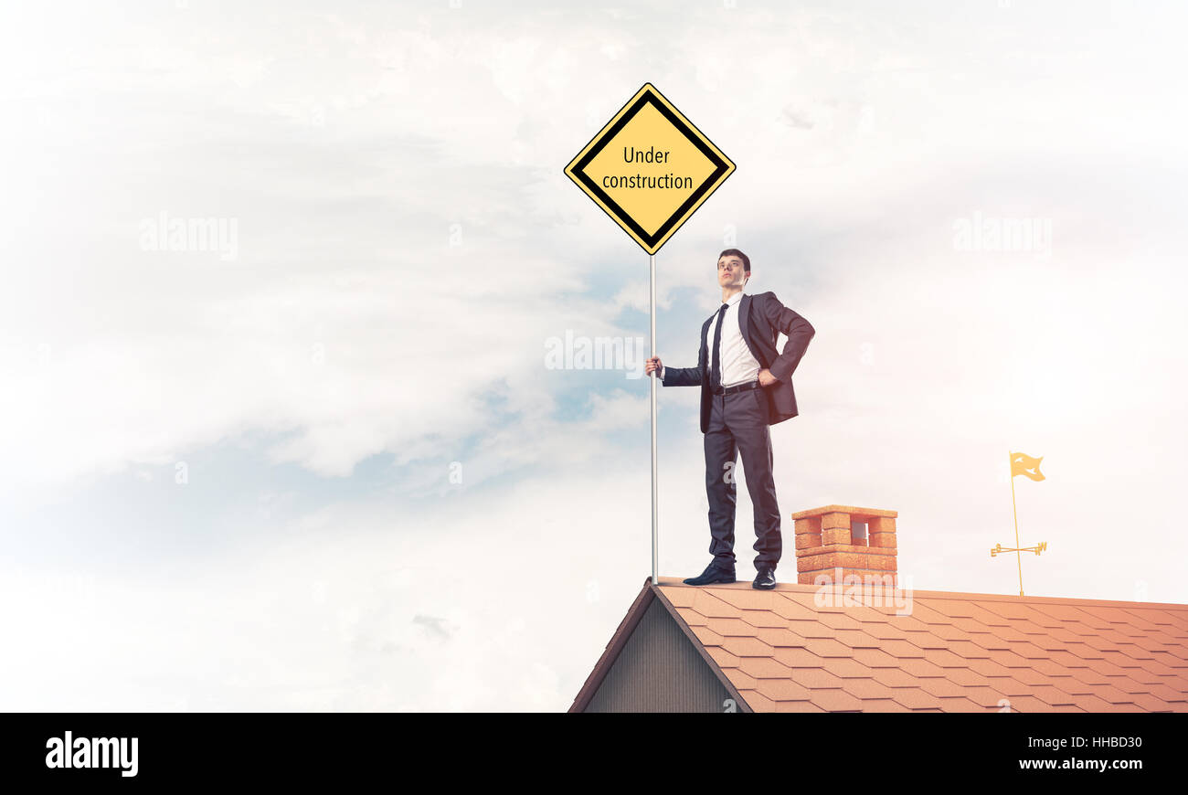 Young businessman on house brick roof holding yellow signboard Stock ...