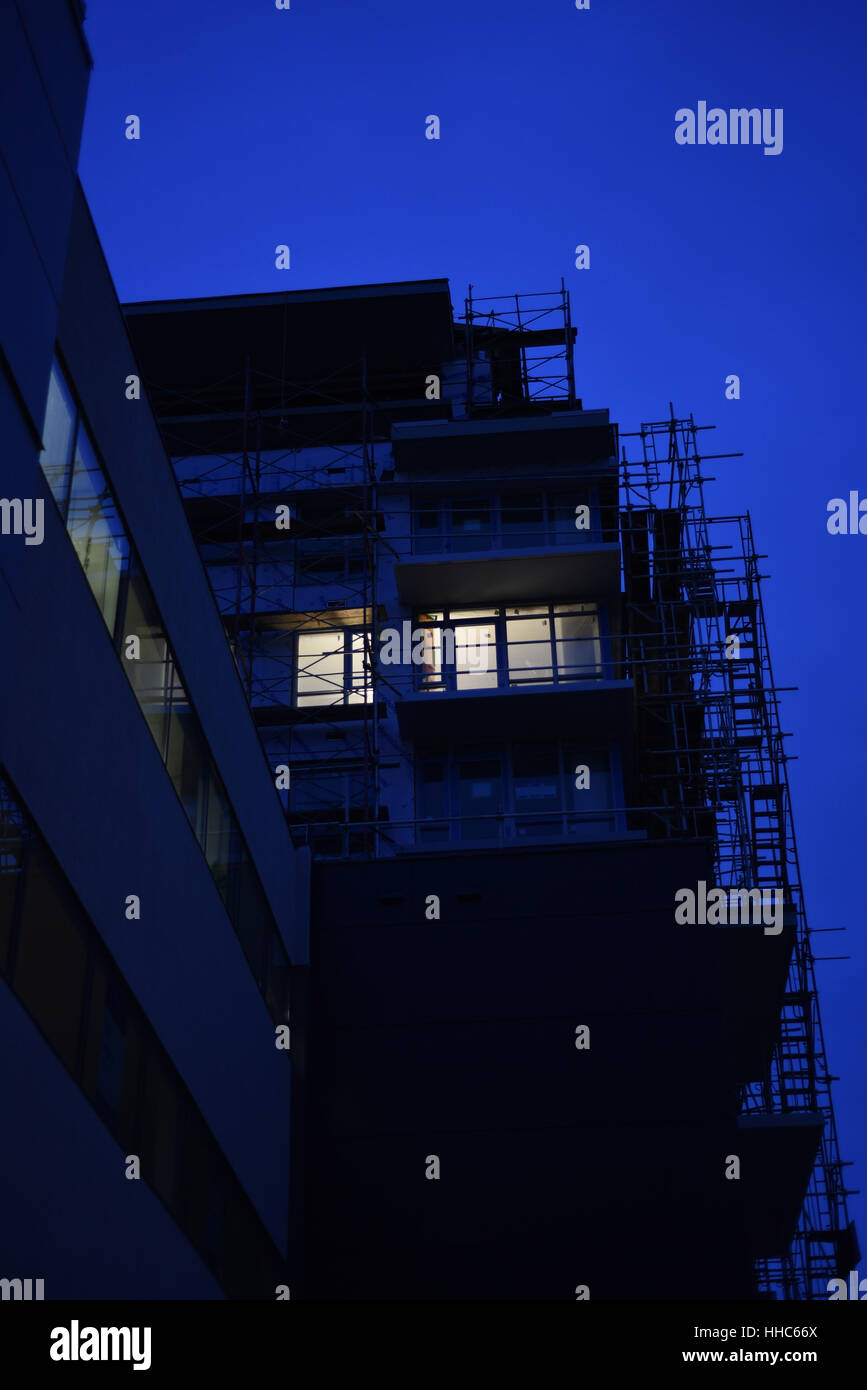 A light glows through windows in a building, covered in scaffolding ...