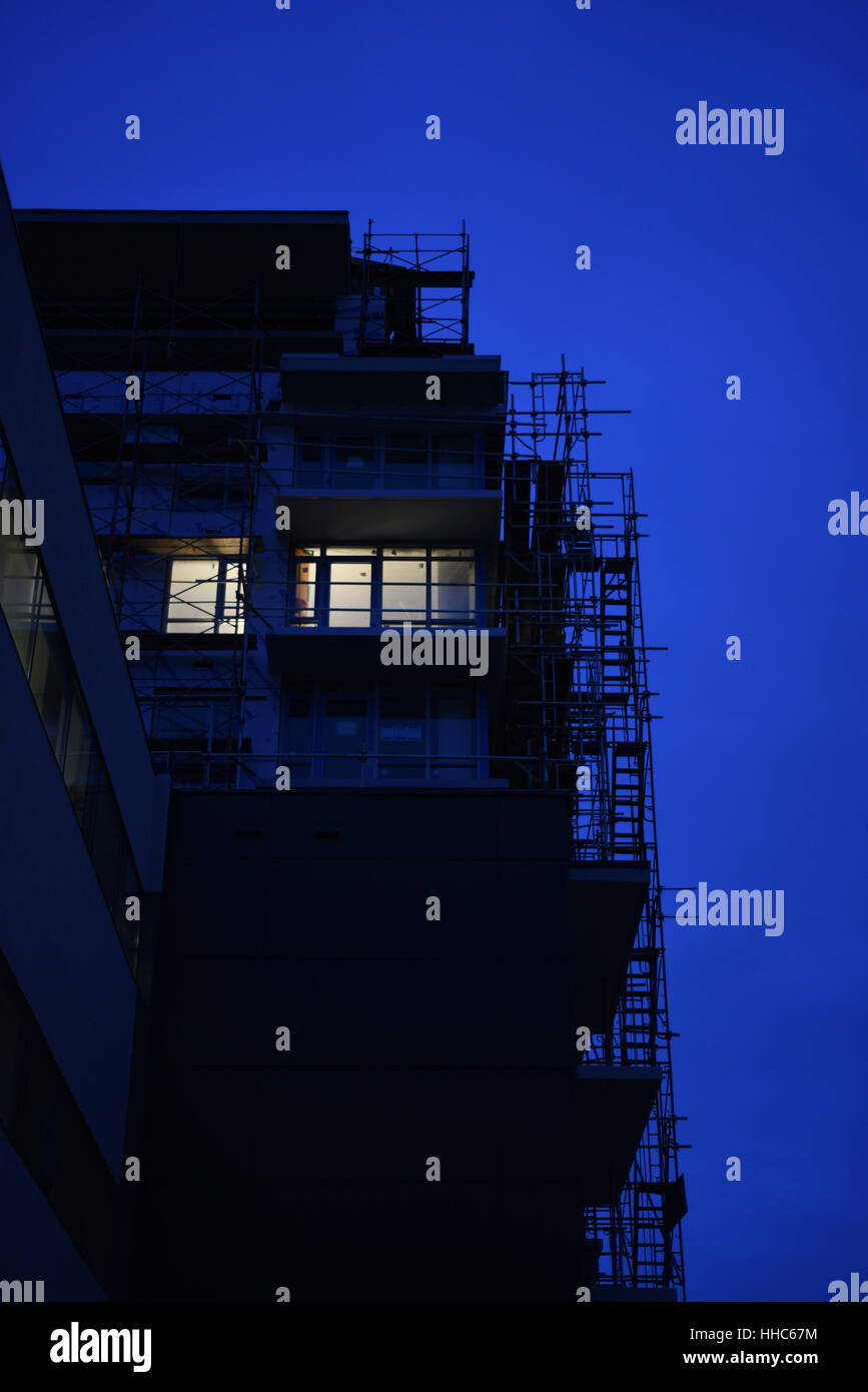 A light glows through windows in a building, covered in scaffolding ...