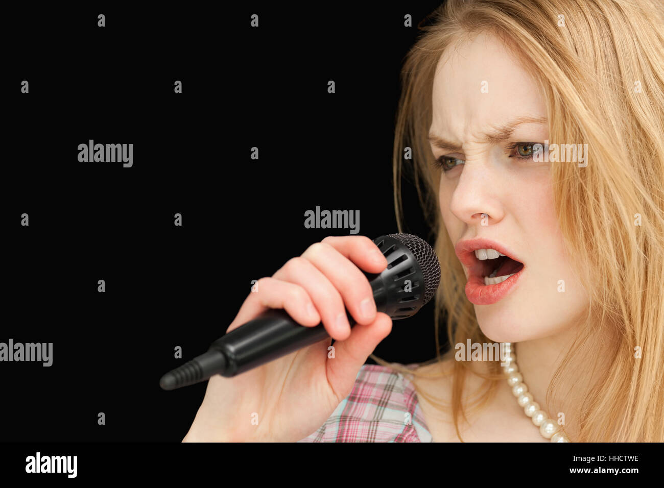 Woman singing while frowning against black background Stock Photo - Alamy
