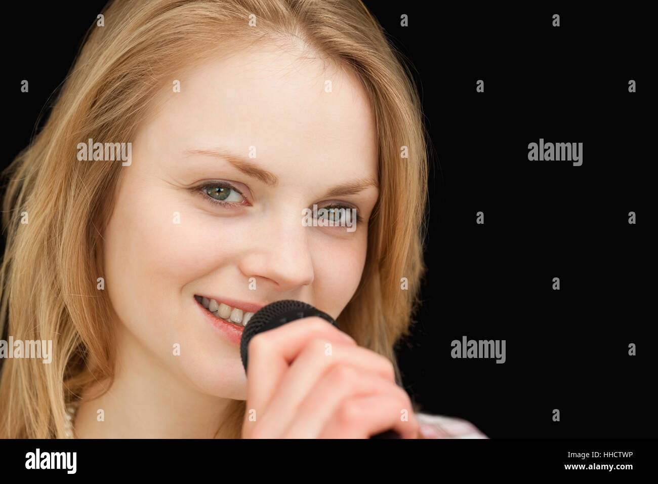 Young woman smiling while singing against black background Stock Photo ...
