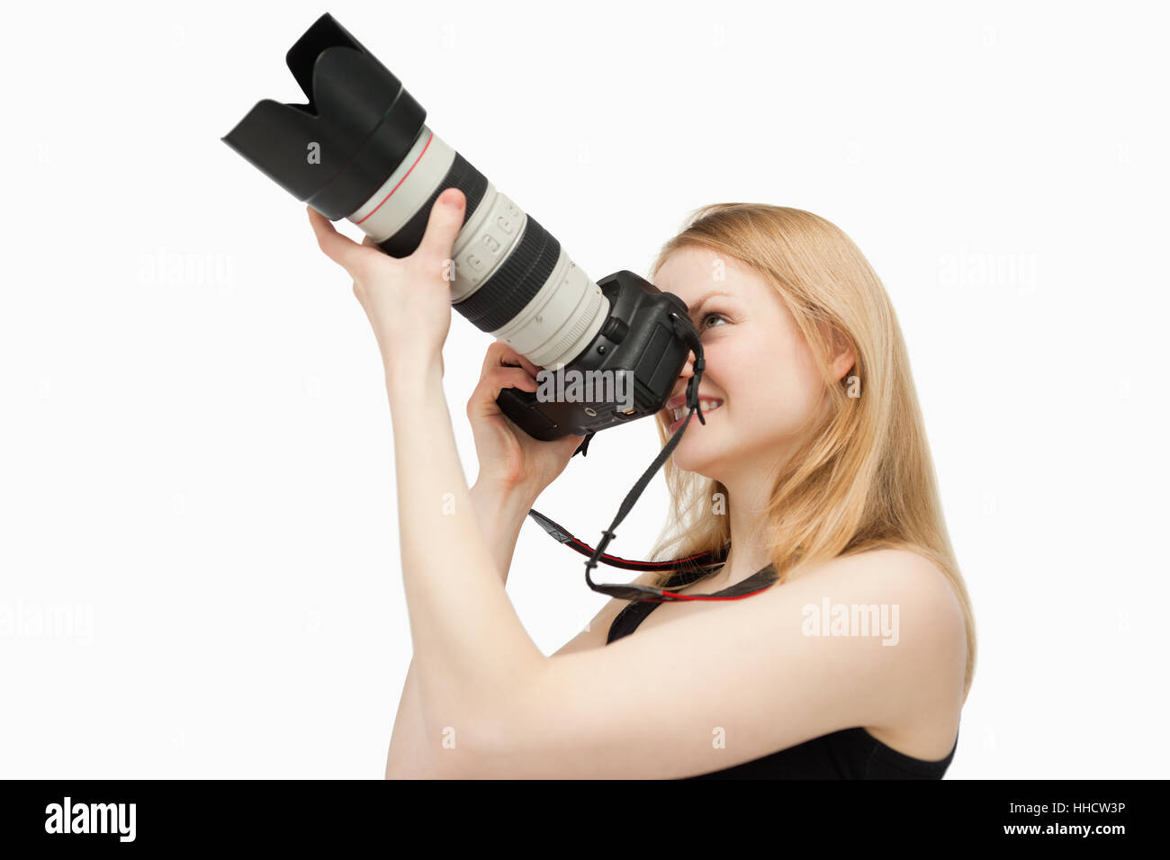 Woman aiming with a SLR camera while smiling against white background ...