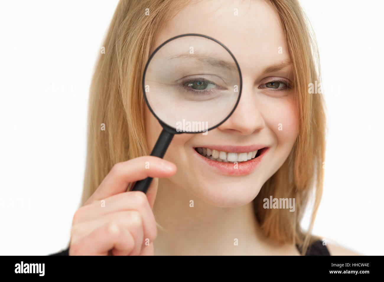 Woman placing a magnifying glass on her eye against white background ...