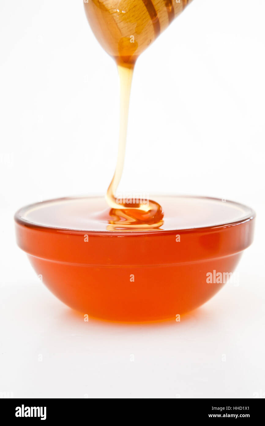 Honey trickle dropping in full honey bowl against a white background ...
