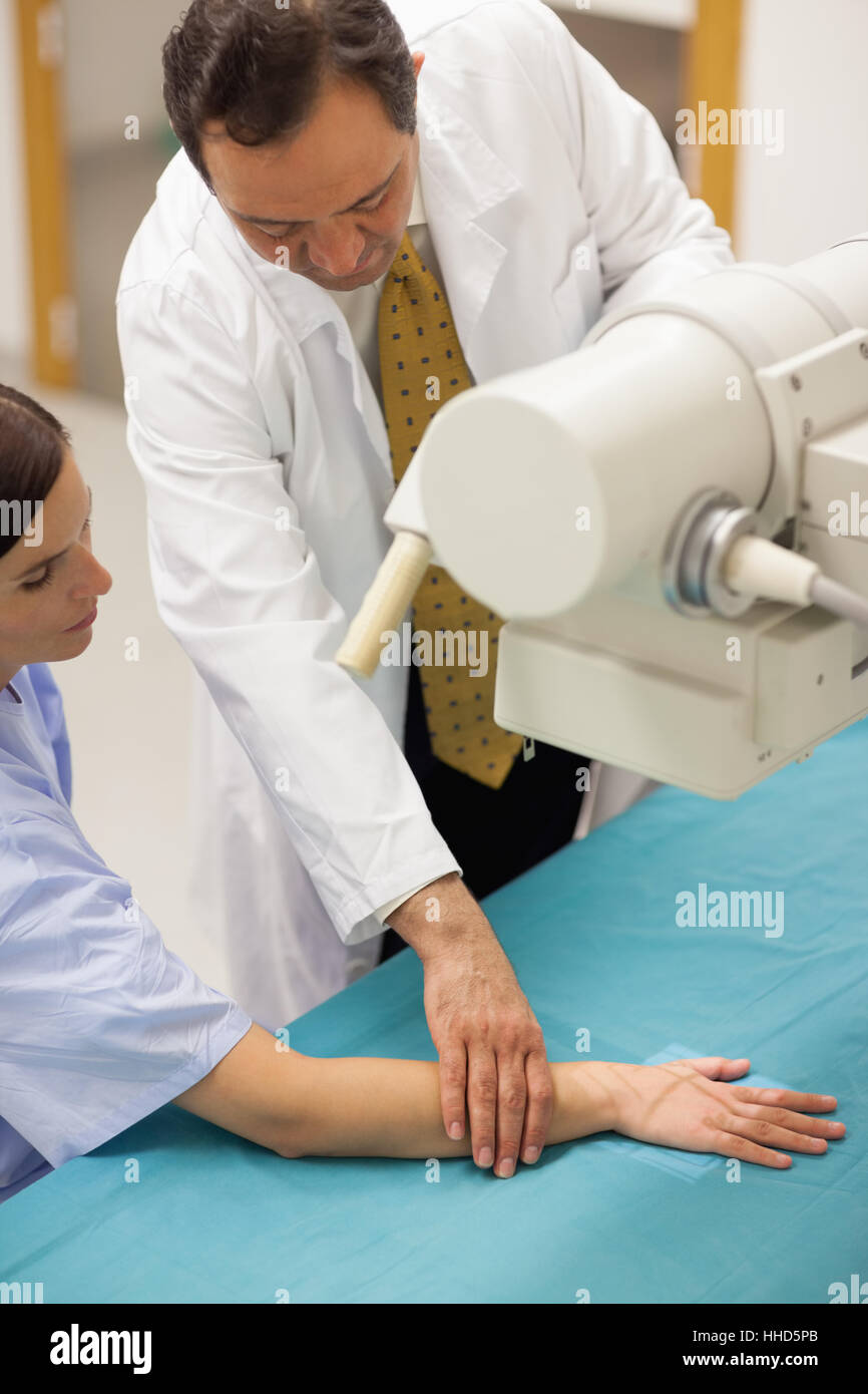 Doctor placing the arm of a patient on a table in a radiography room ...