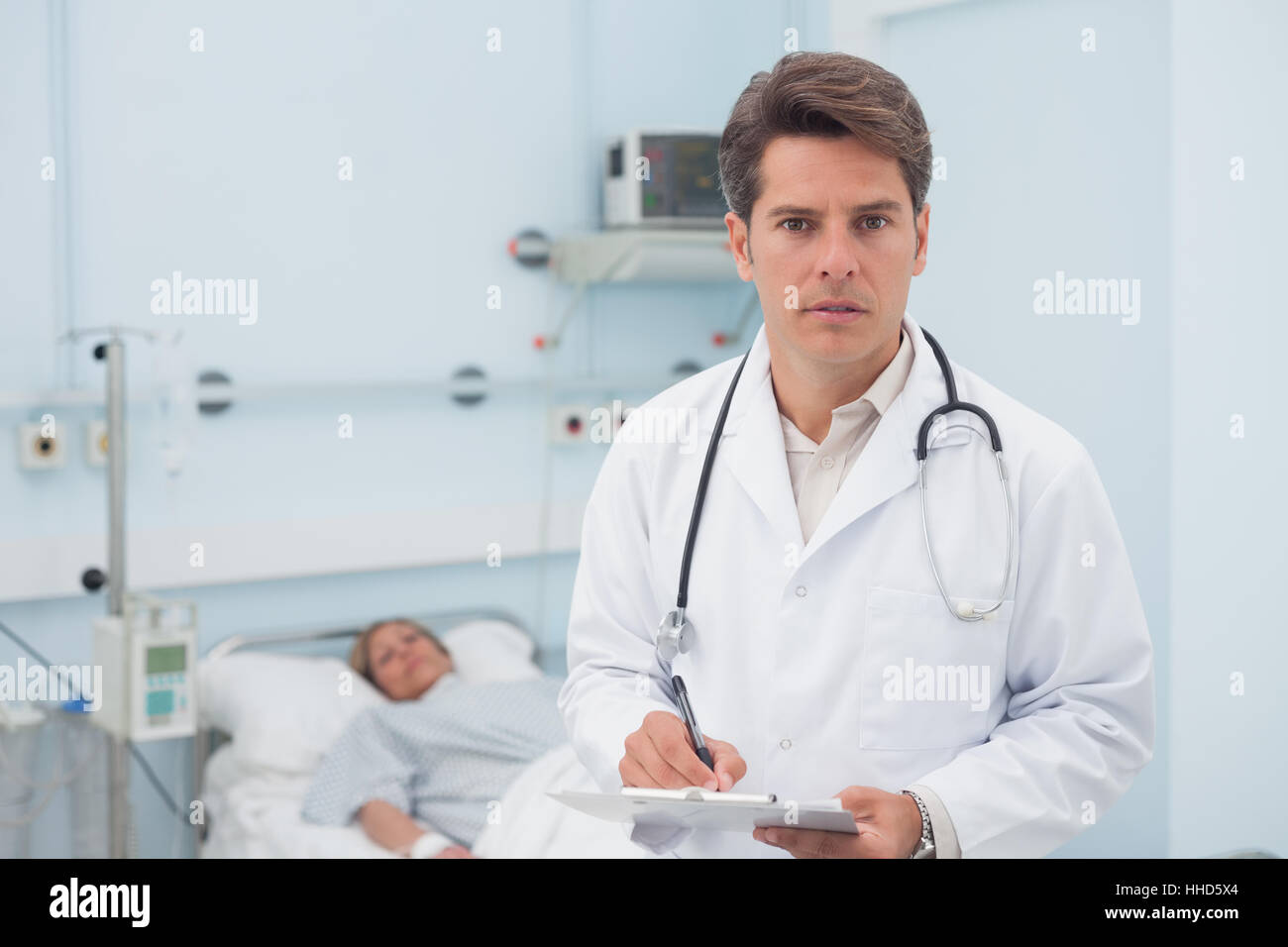 Doctor writing while holding a chart in hospital ward Stock Photo - Alamy
