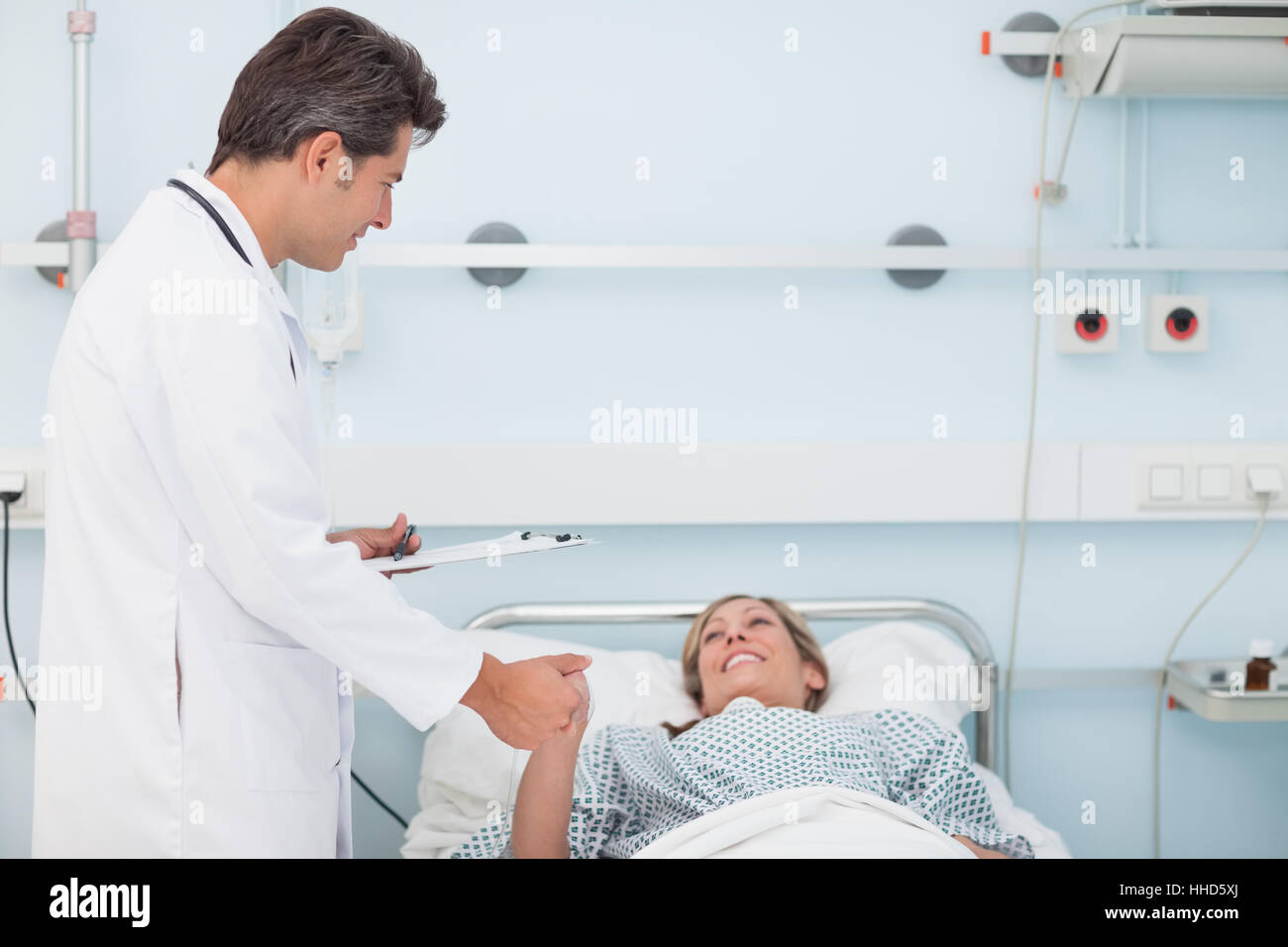 Doctor looking at his patient while holding her hand in hospital ward ...