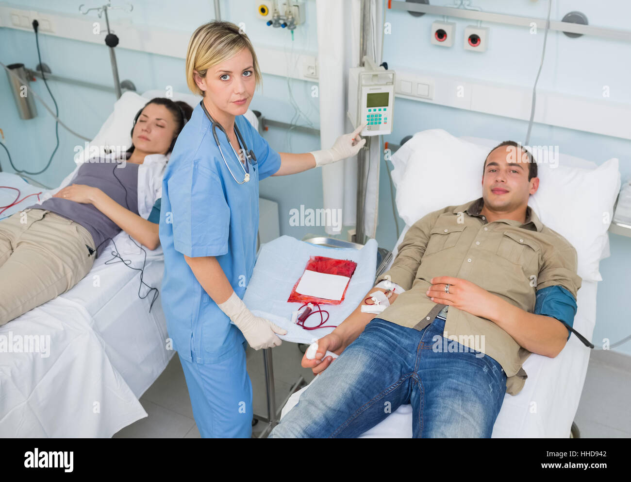 Nurse touching monitor next to transfused patients in hospital ward ...