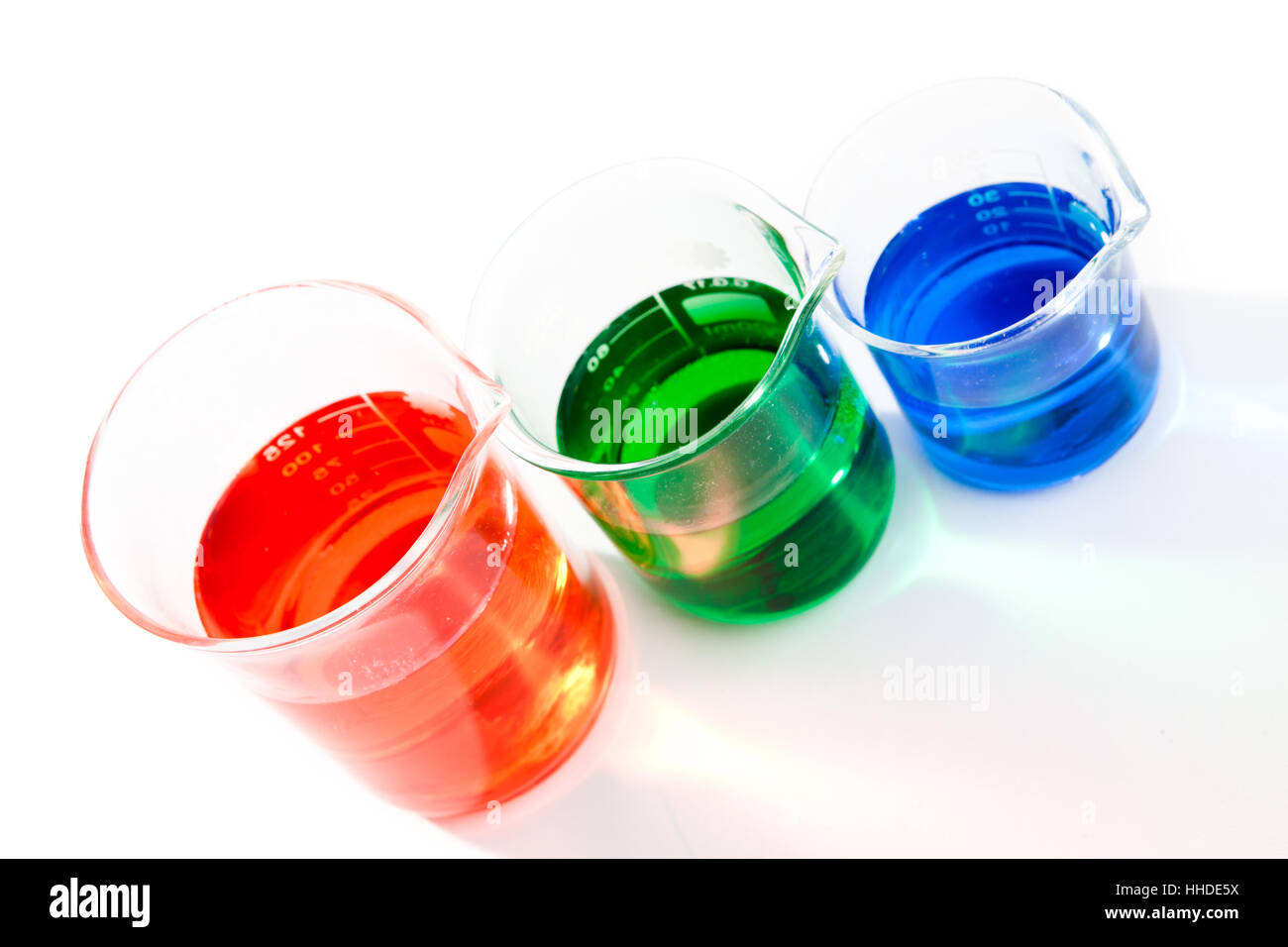 Three beakers of different colour and size against a white background ...