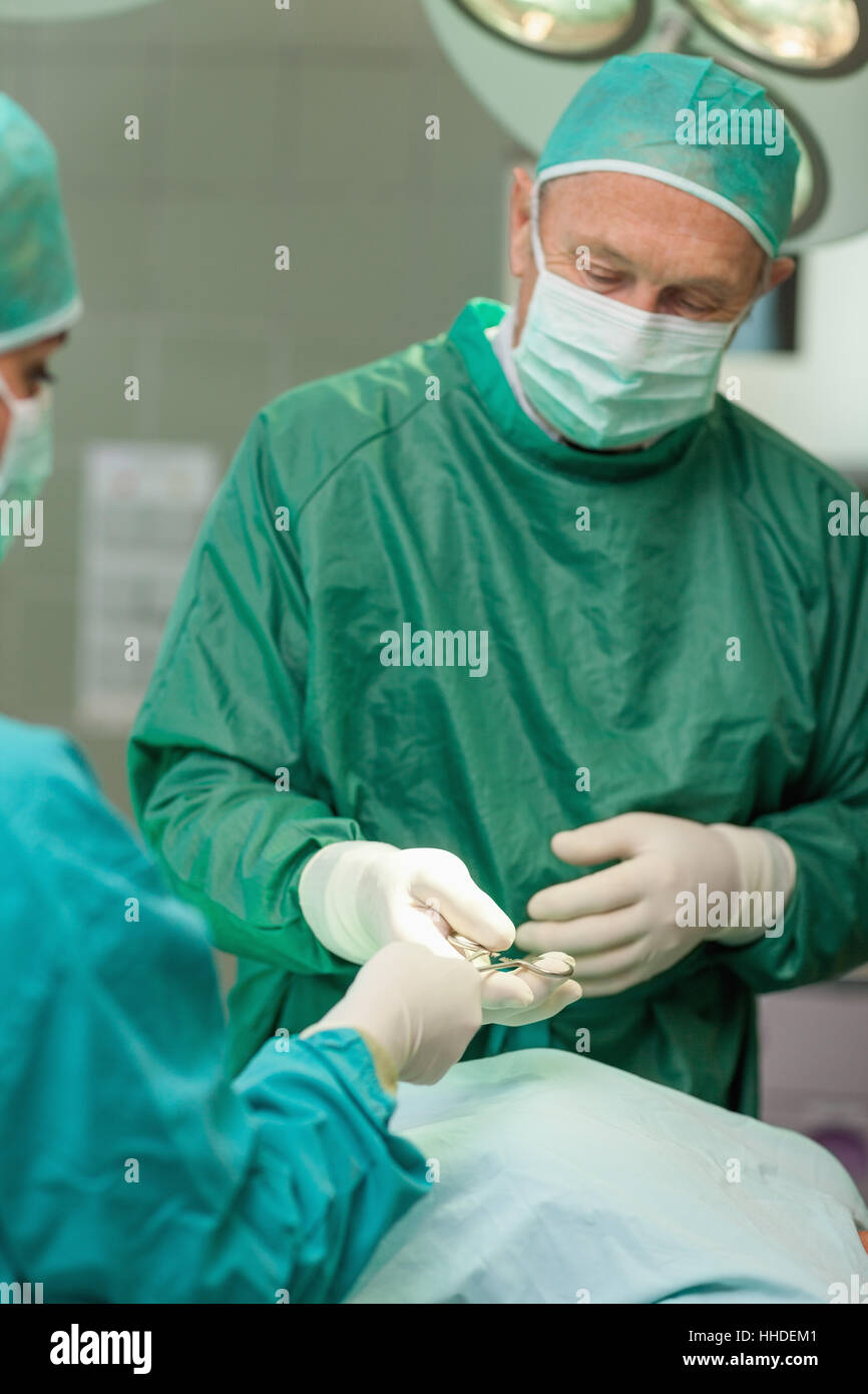 Surgeon giving a scissors to an other surgeon in a surgical room Stock ...