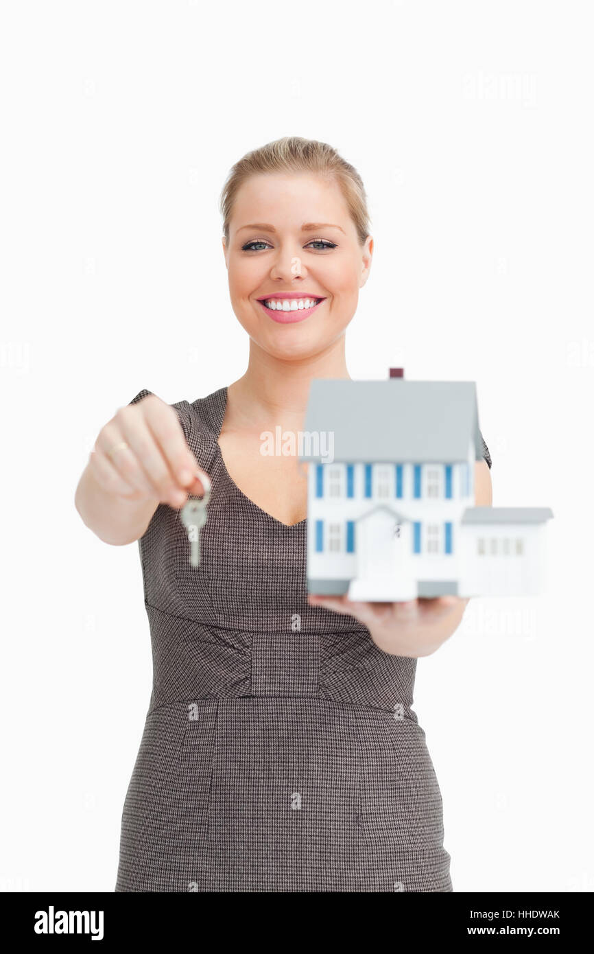 Woman smiling showing a model house and a key against white background ...